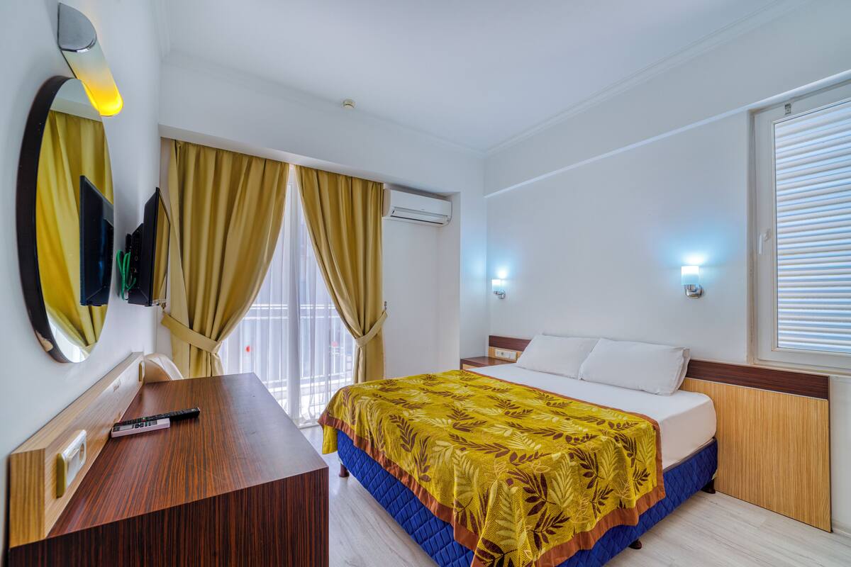 Quarto de hotel com cama, escrivaninha, televisão e ar condicionado.