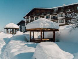 Uma área externa coberta de neve, com um coreto de madeira e um edifício com varandas.