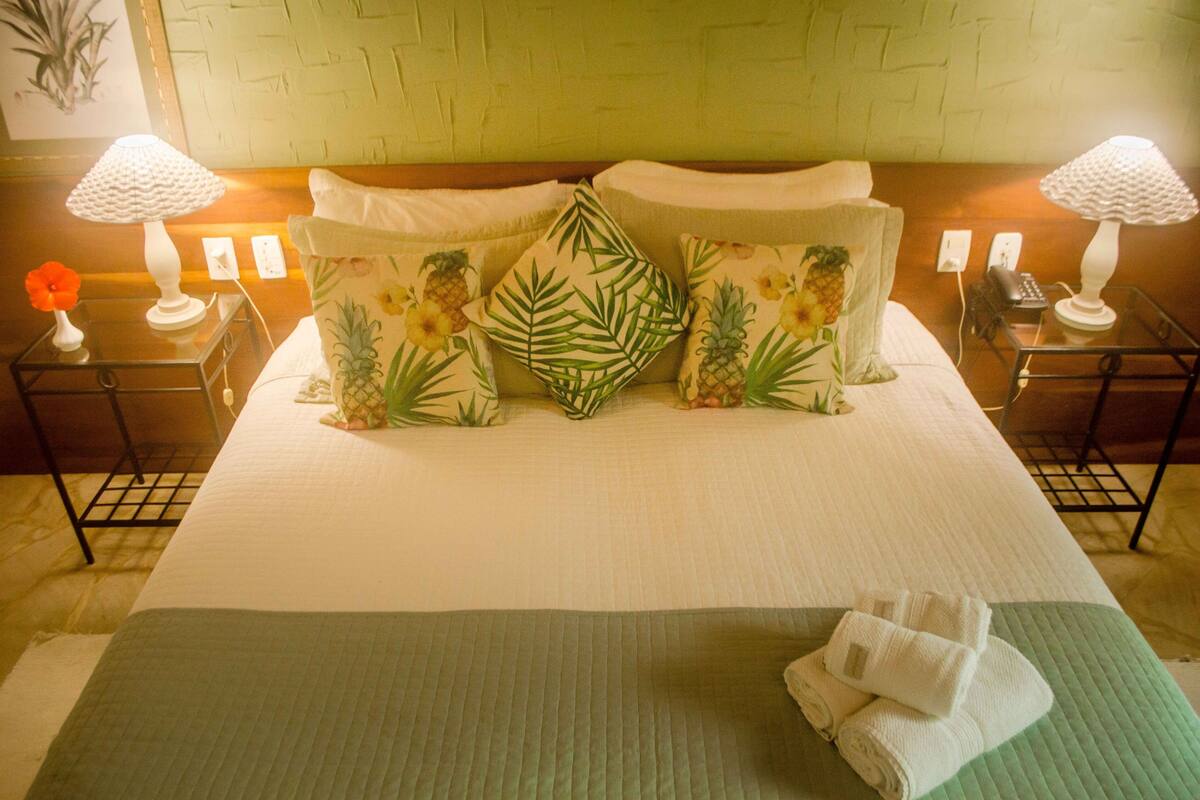 Cama bem arrumada com almofadas florais, duas mesas de cabeceira com abajures e um edredom acolchoado verde.
