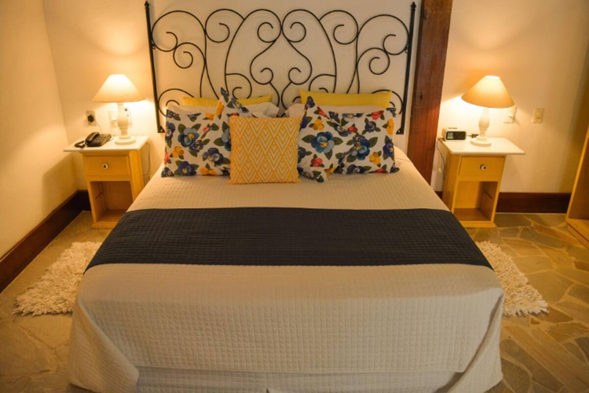 Cama bem arrumada com almofadas florais, duas mesas de cabeceira com abajures e uma cabeceira decorativa de metal.