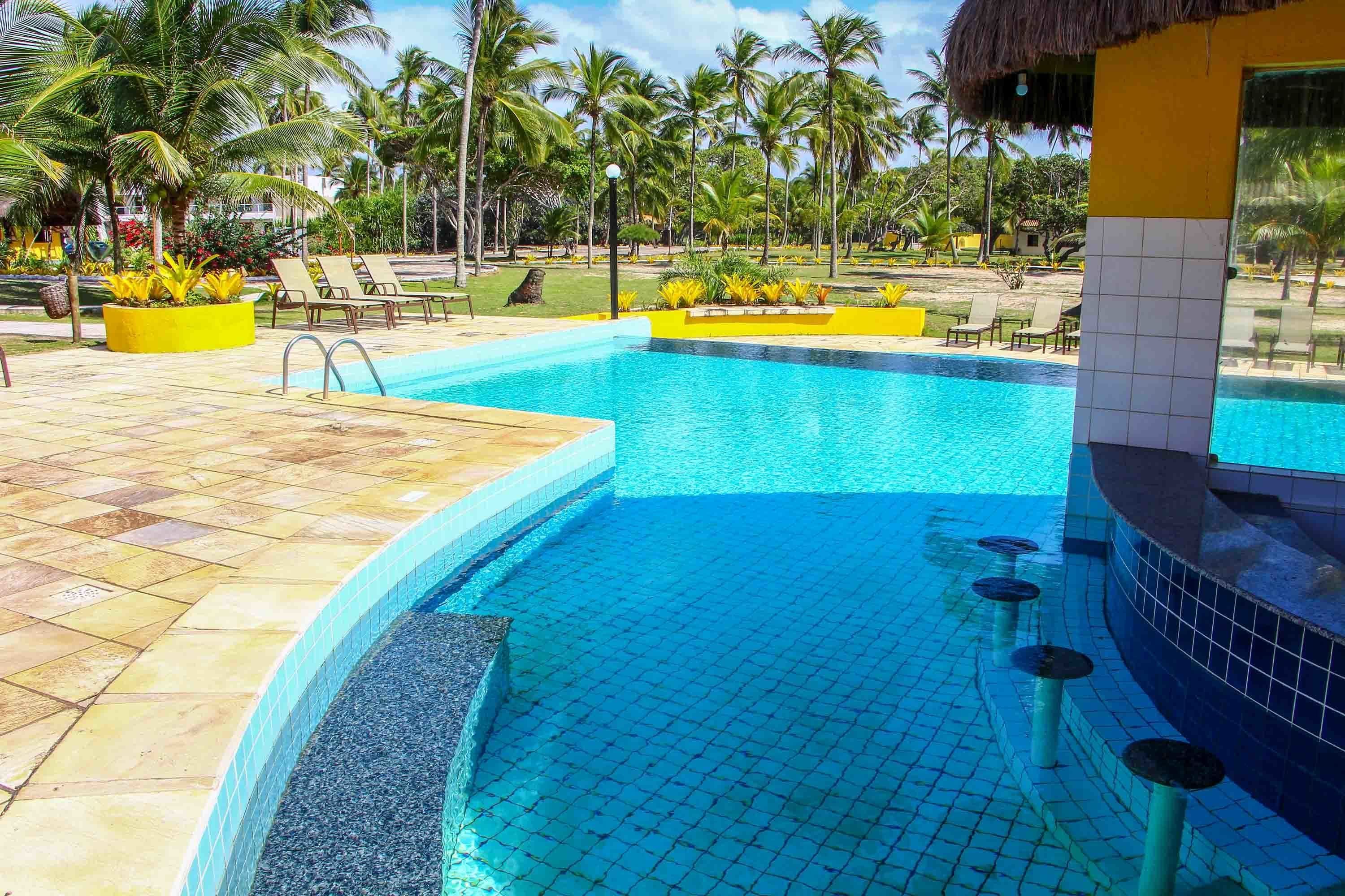 Uma piscina com bordas azulejadas, cadeiras de descanso e plantas em vasos.