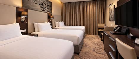 Quarto de hotel com duas camas, uma escrivaninha, televisão de tela plana e obras de arte nas paredes.