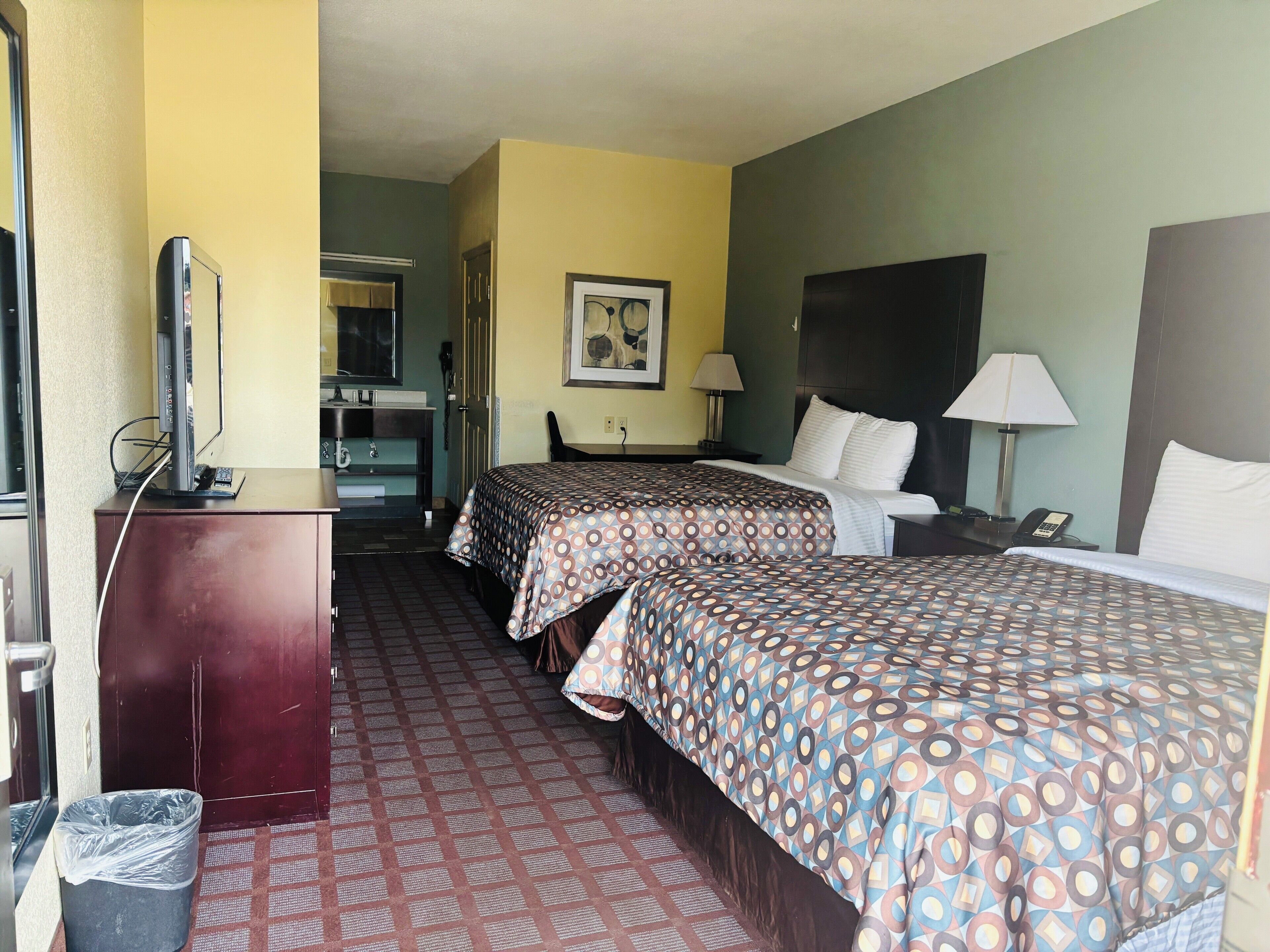 Quarto de hotel com duas camas, uma escrivaninha, uma cadeira, uma televisão e banheiro.