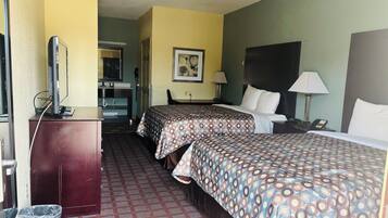Quarto de hotel com duas camas, uma escrivaninha, uma cadeira, uma televisão e banheiro.