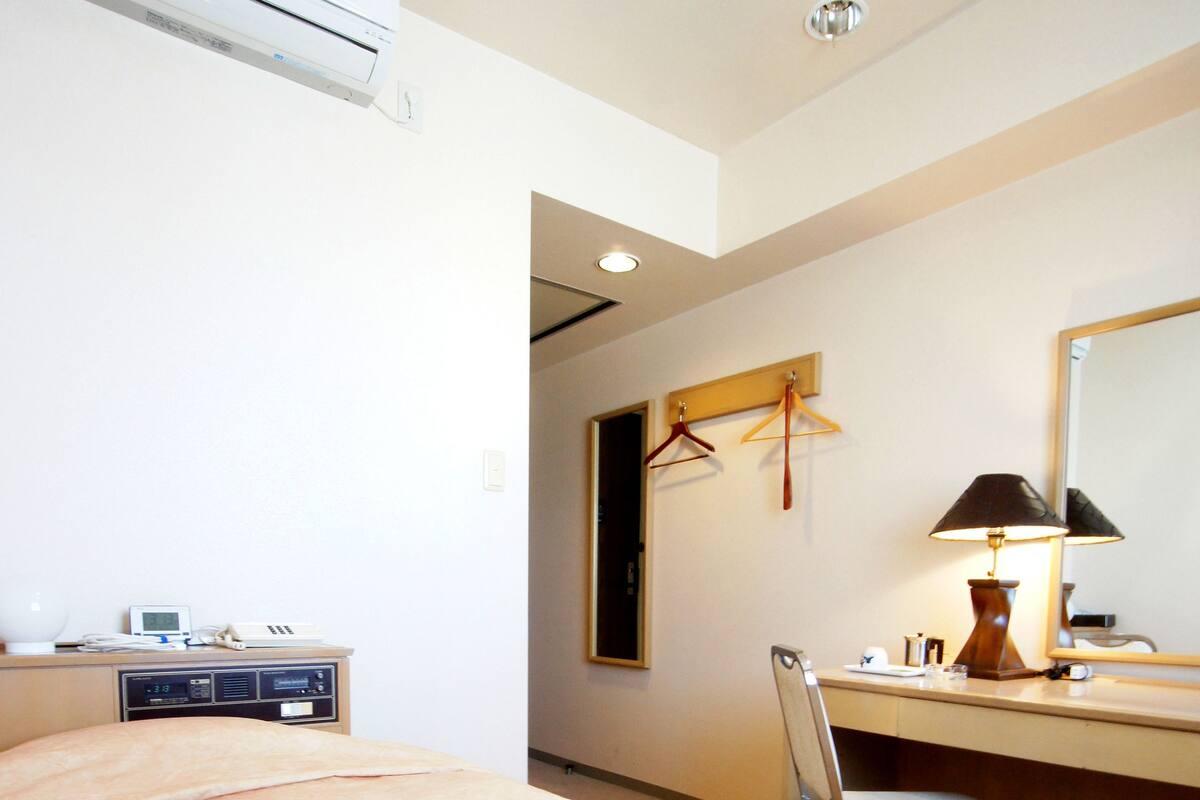 Quarto de hotel com cama, escrivaninha, cadeira, ar condicionado, luminária e espelho.