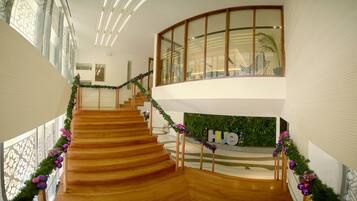 Interior com vários níveis, escada de madeira, guarda-corpos de vidro e decorações festivas.