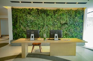 Balcão de recepção com dois monitores Acer, um vaso com flores e um painel vertical com jardim verde.