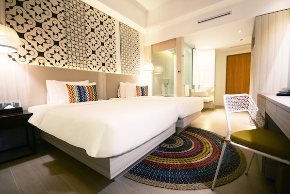 Quarto de hotel com uma cama grande, uma escrivaninha, uma cadeira e um banheiro visível por uma porta aberta.