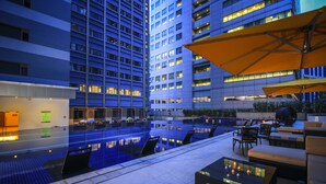 Uma área de piscina moderna em hotel, com vista clara para a piscina, espreguiçadeiras e guarda-sóis.