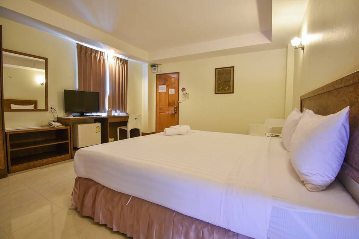 Quarto de hotel com uma cama grande, uma escrivaninha com televisão, um espelho e uma porta com placa.