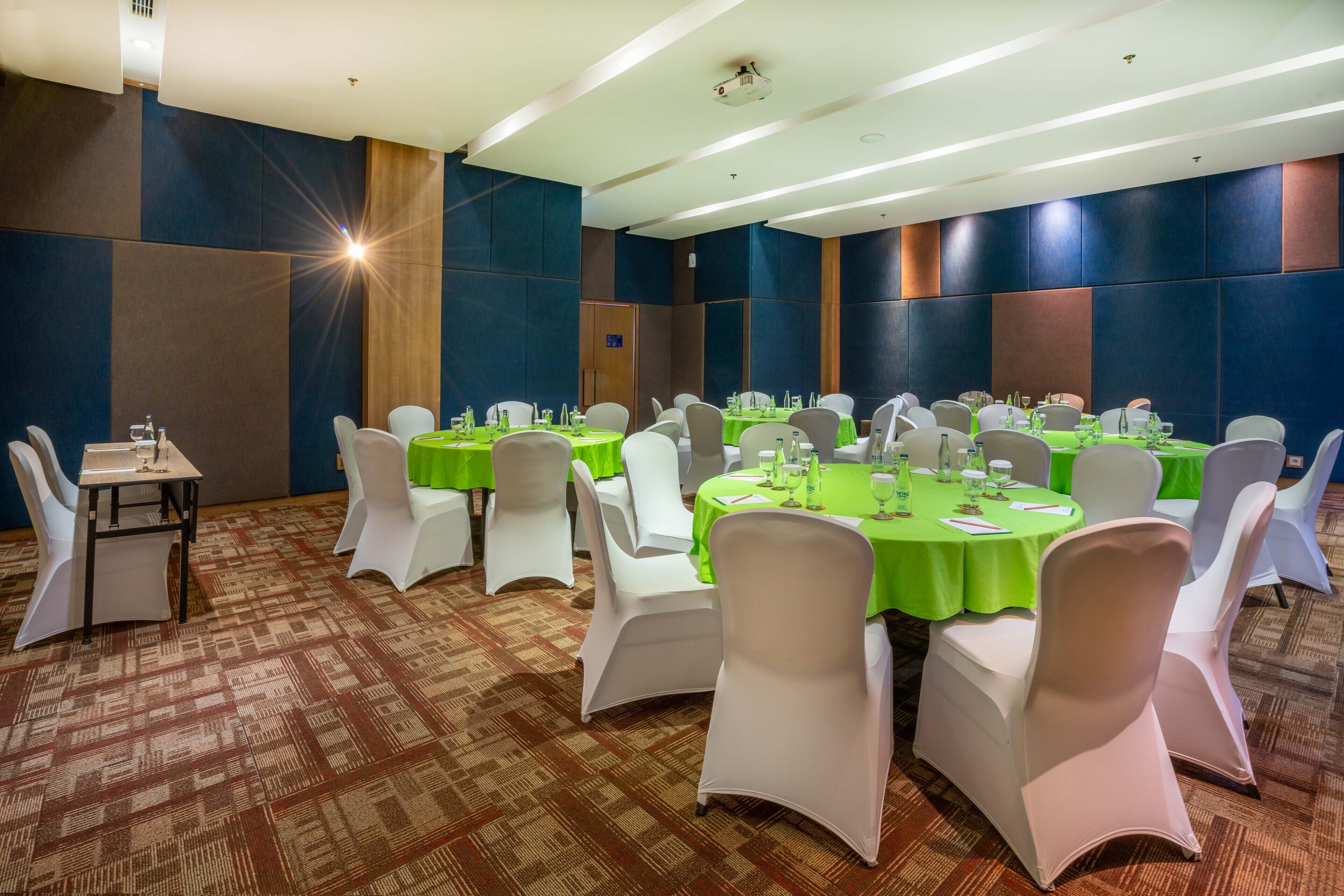 Uma sala de conferências com mesas redondas, cadeiras brancas e toalhas de mesa verdes.