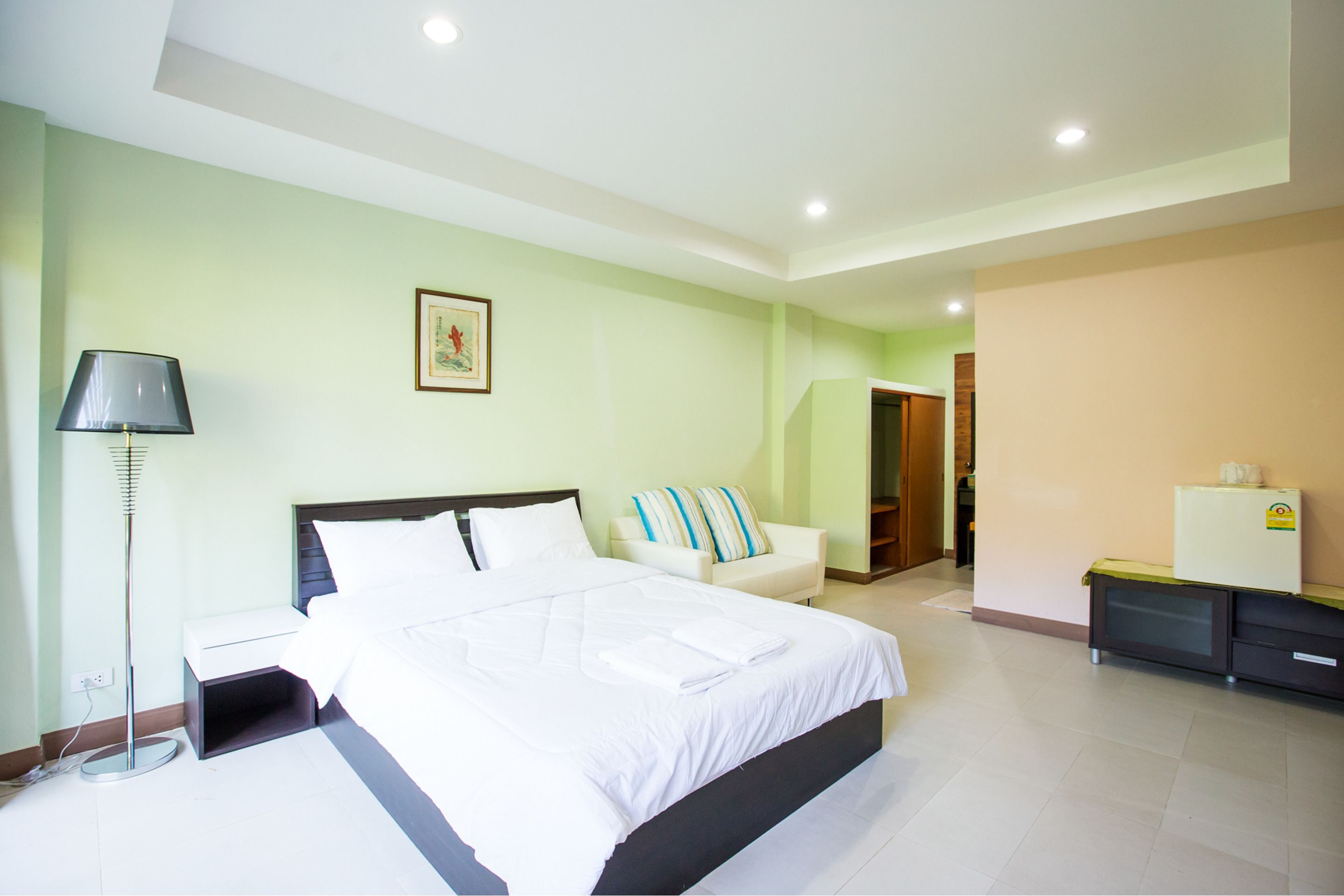 Quarto de hotel com uma cama grande, uma mesinha de cabeceira, um abajur, um sofá e um pequeno armário.