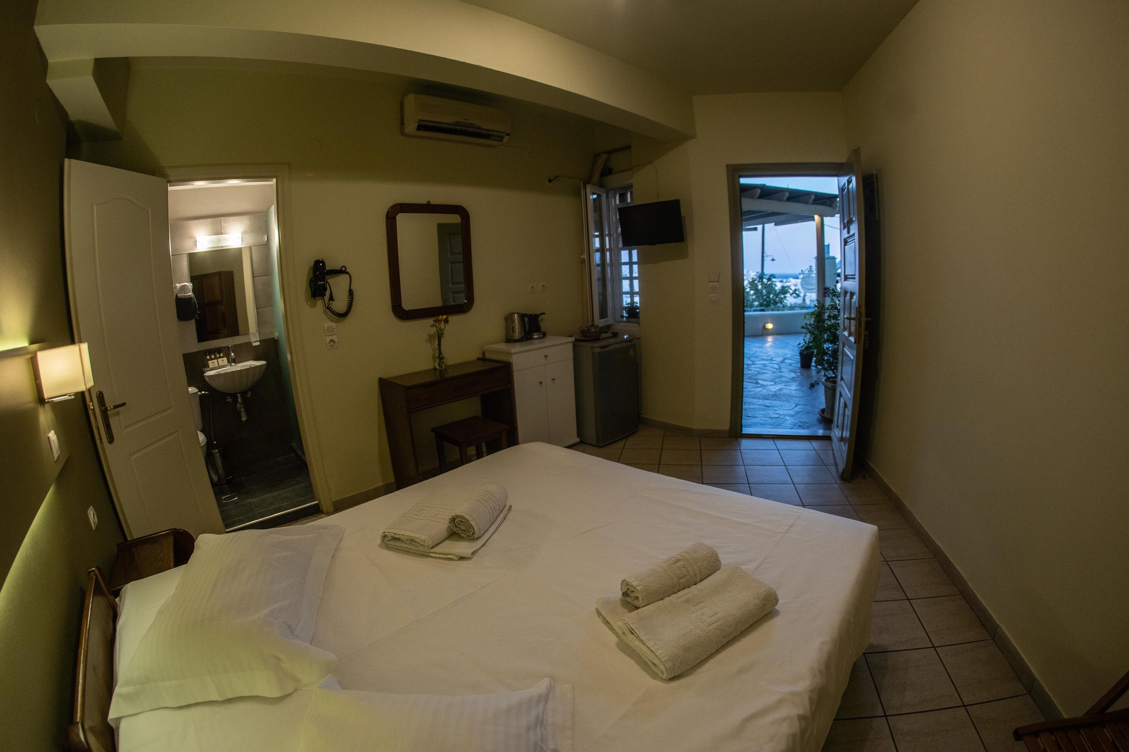Quarto de hotel com cama, banheiro, escrivaninha e televisão.