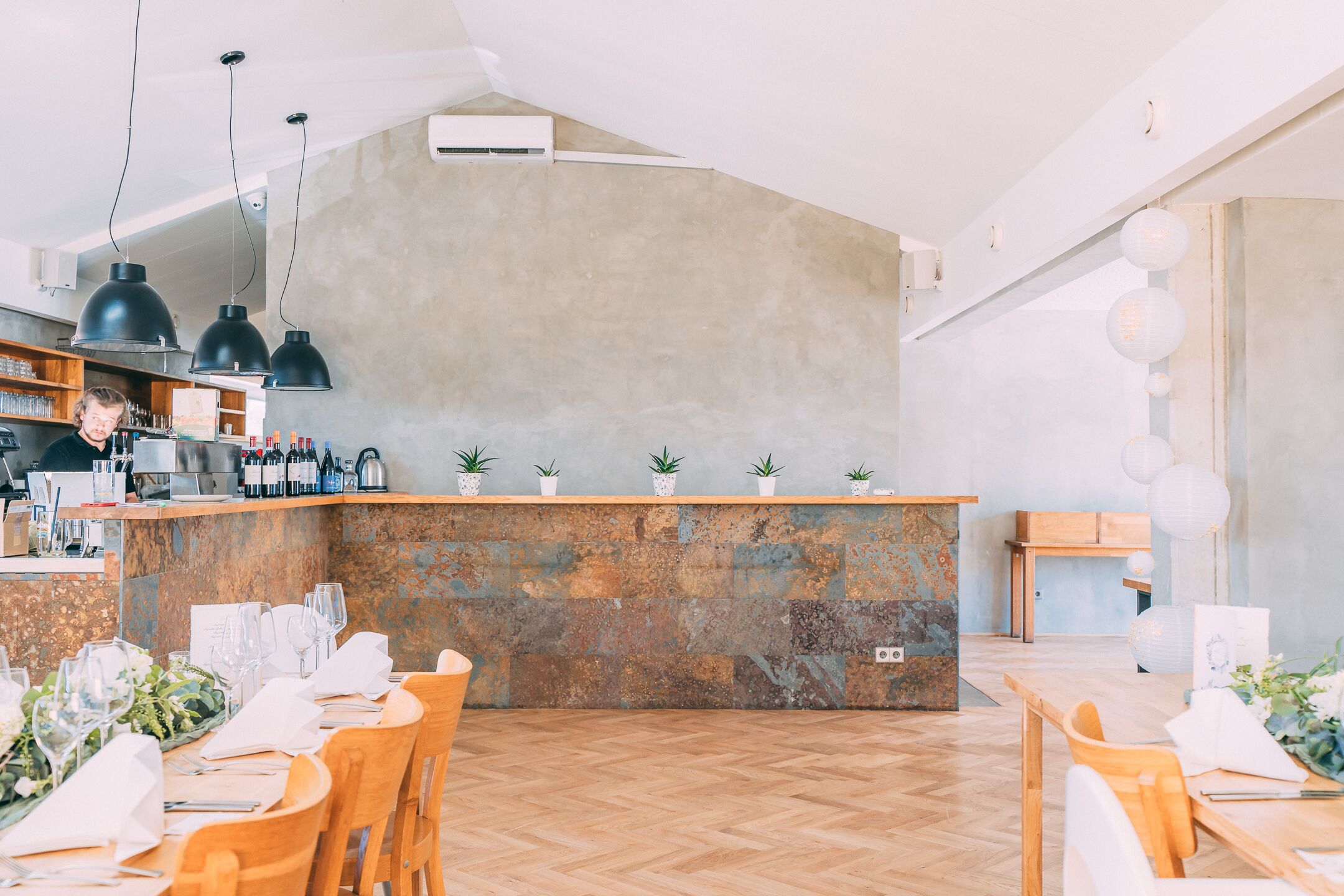 Um restaurante moderno com balcão de pedra rústica, mesas de madeira e luminárias pendentes.