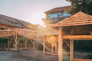 Uma estrutura de madeira para brincar com escorrega e elementos de escalada, ao lado de um edifício com varanda.