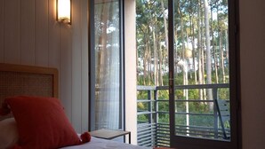 Quarto de hotel com cama, janela com vista para árvores e luminária fixada na parede.