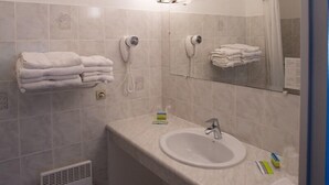 Casa de banho moderna com lavatório branco, espelho, suporte de toalhas e secador de cabelo.