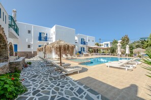 Uma área de piscina com espreguiçadeiras, um guarda-sol de palha e um caminho de pedra.