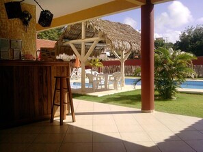 Uma área externa coberta com um bar, cadeiras e uma piscina.
