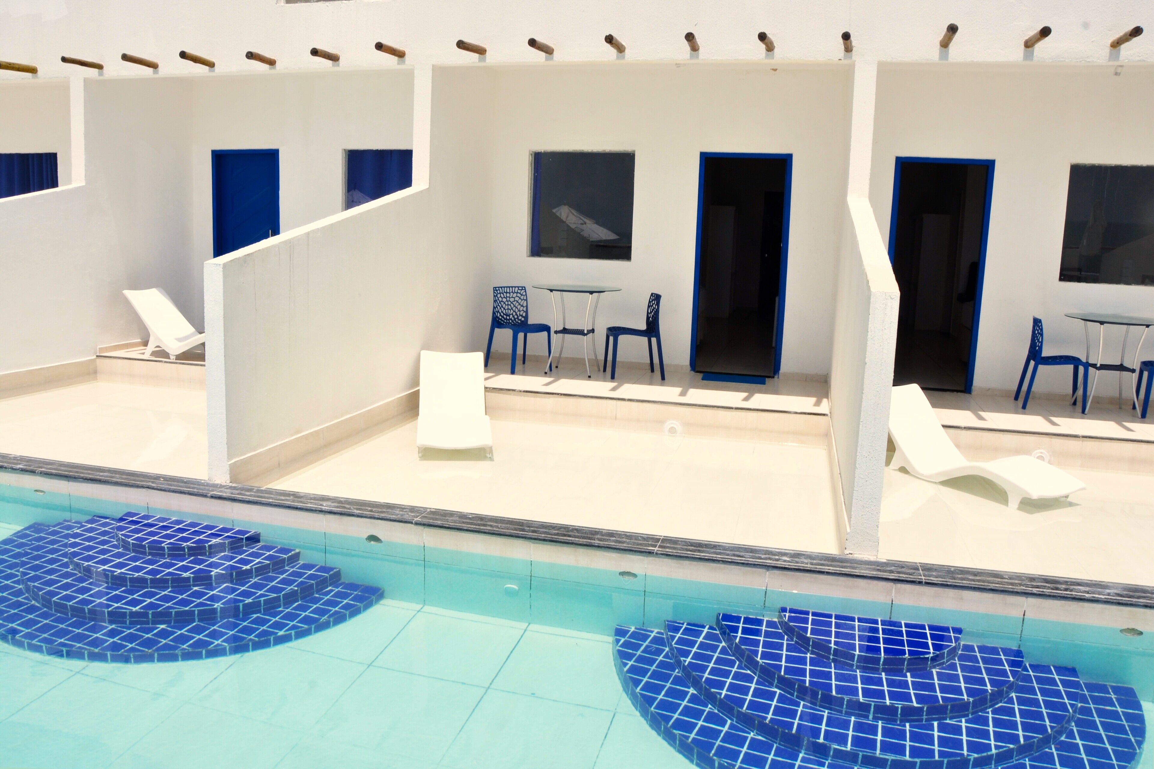 Área de piscina com degraus azulejados, espreguiçadeiras brancas e cadeiras azuis.