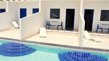 Área de piscina com degraus azulejados, espreguiçadeiras brancas e cadeiras azuis.