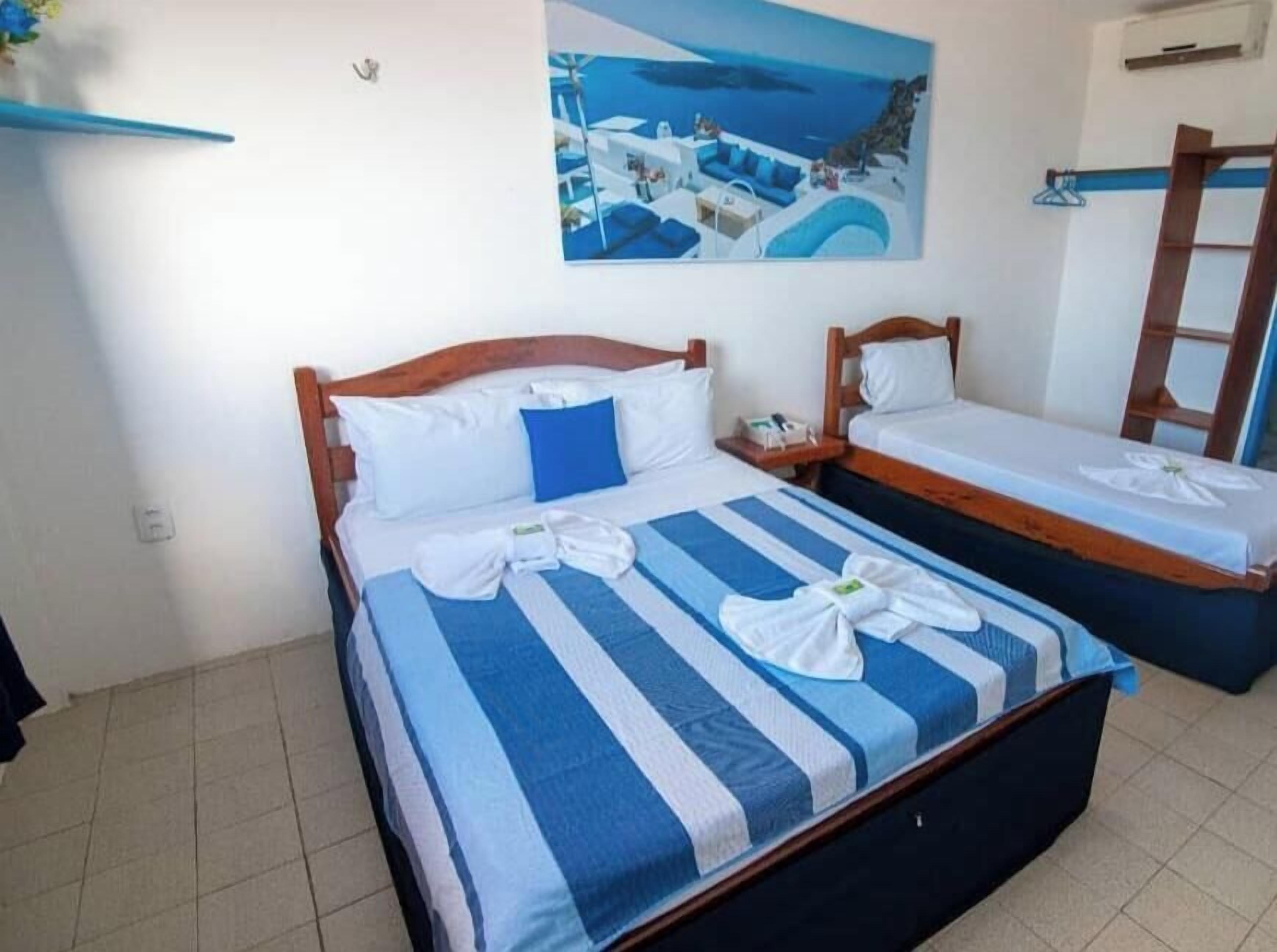 Quarto de hotel com duas camas, um quadro de uma paisagem costeira e uma escada de madeira.