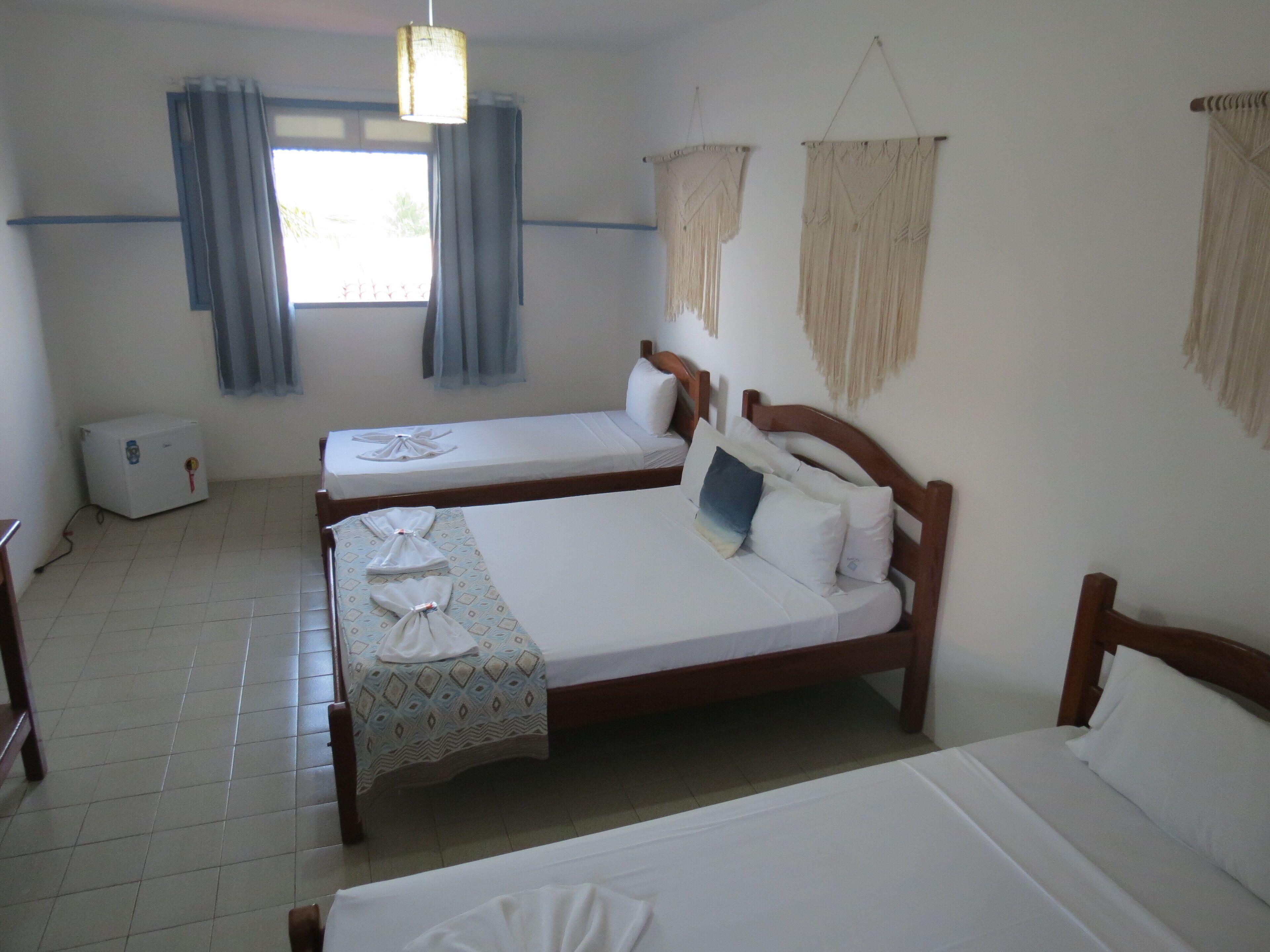 Quarto com duas camas de solteiro, uma mesinha, aquecedor e janela com cortinas.