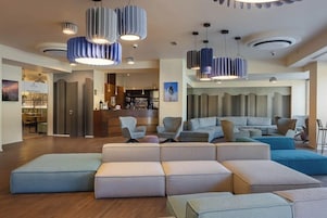 A modern hotel lobby with a seating area, a bar, and a reception desk.