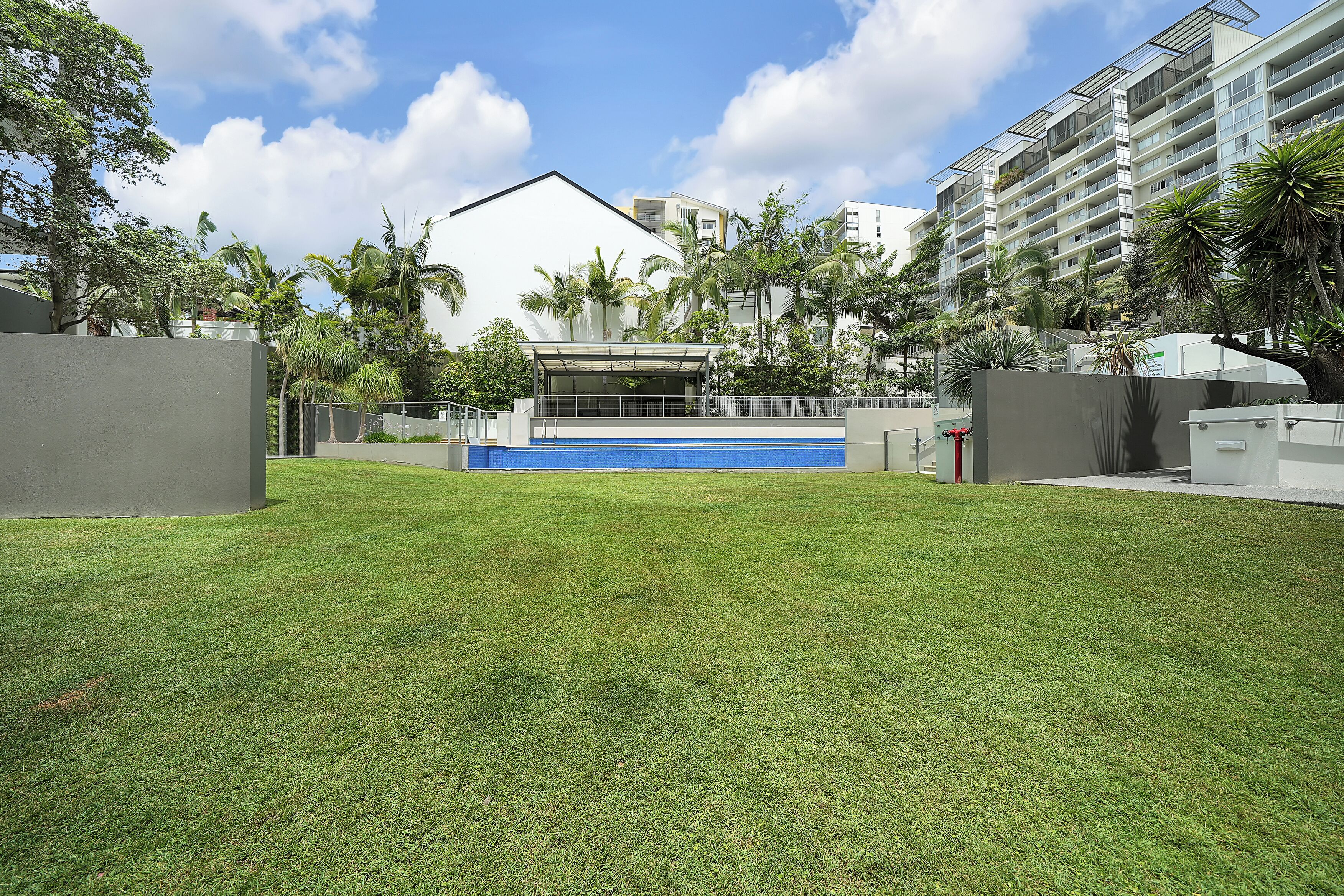 Um pátio moderno de hotel com piscina, palmeiras e um edifício branco com varandas.