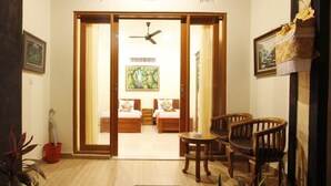 Quarto de hotel com piso de madeira, uma cama com cabeceira, uma escrivaninha com cadeira e uma pequena mesa com duas cadeiras.