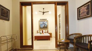 Quarto de hotel com cama, ventilador de teto, um quadro na parede e uma pequena mesa com cadeiras.