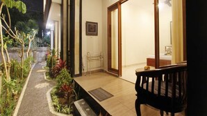 Entrada de hotel com um banco de madeira, um pequeno jardim e uma porta de vidro deslizante para um quarto.