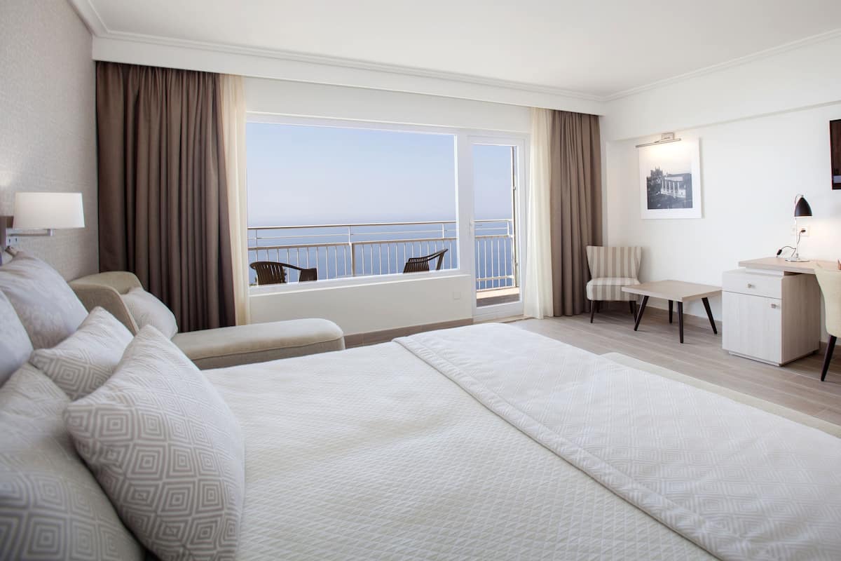 Quarto de hotel com uma cama grande, uma escrivaninha, uma cadeira e vista para o mar.