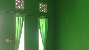 Quarto com paredes verdes, cama com roupa de cama branca, duas almofadas e uma toalha enrolada.