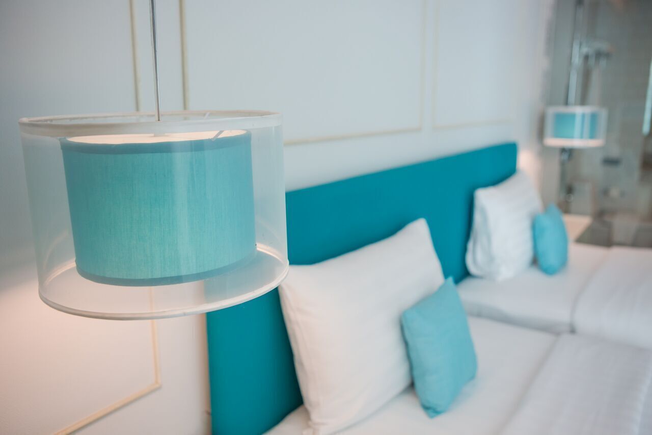 Quarto moderno com cabeceira verde-água, roupa de cama branca e abajur com cúpula azul.