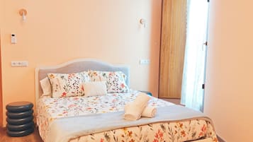 Cama bem arrumada com roupa de cama florida, mesa de cabeceira e porta de madeira em um quarto com paredes cor de pêssego.