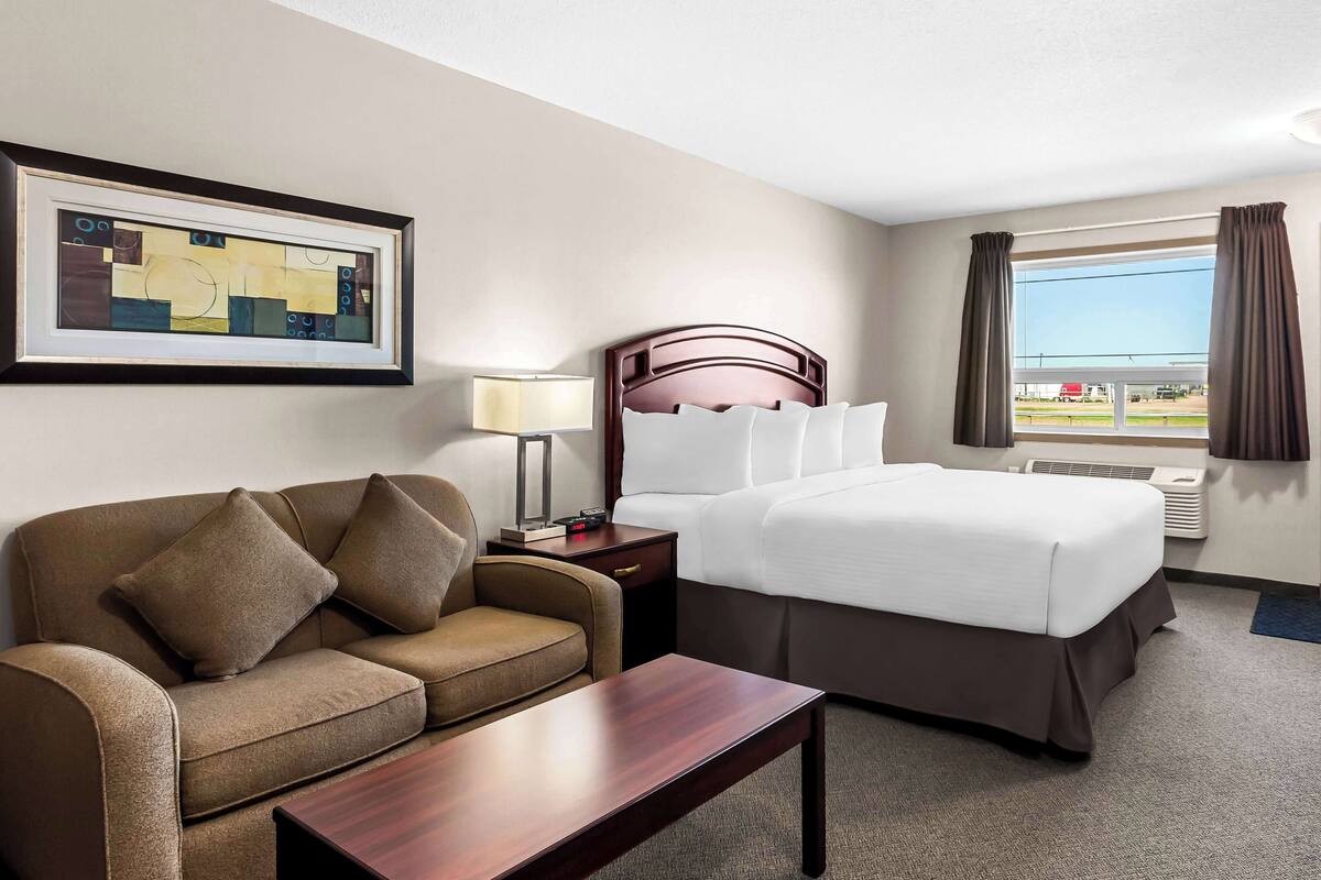 Quarto de hotel com cama, sofá, mesa de cabeceira, luminária e quadro na parede.
