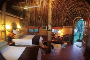 Quarto com duas camas, uma mesa de madeira, uma cadeira, lareira e uma grande porta em arco que dá para o exterior.