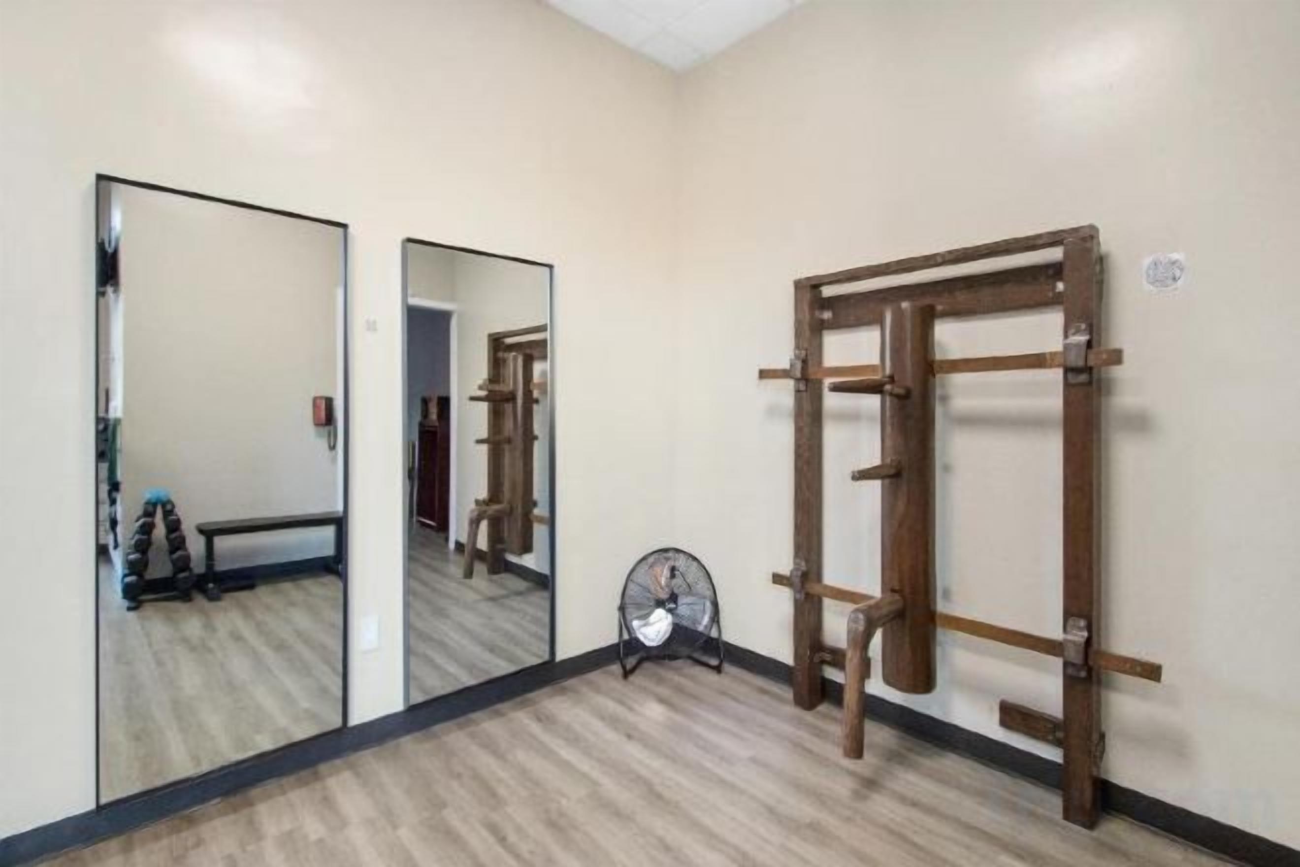 Quarto com espelho grande, porta-roupas de madeira e ventilador.