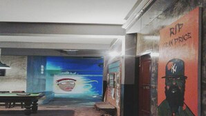 Um corredor com mesa de bilhar, um mural com um rosto e um cartaz na parede.