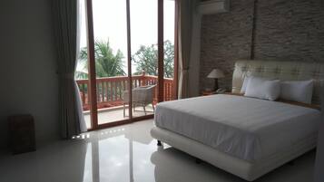 Quarto de hotel com uma cama grande, varanda com uma cadeira de vime e parede de pedra.