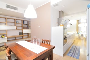 Uma cozinha moderna com eletrodomésticos brancos, uma área de jantar com mesa e cadeiras de madeira e uma estante com diversos objetos.