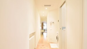 Corredor estreito com um radiador à esquerda, uma máquina de lavar à direita e um tapete estampado no chão.