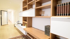 Uma sala de estar moderna com estantes embutidas de madeira, um sofá branco e uma mesa de centro. Há itens decorativos e livros nas estantes.