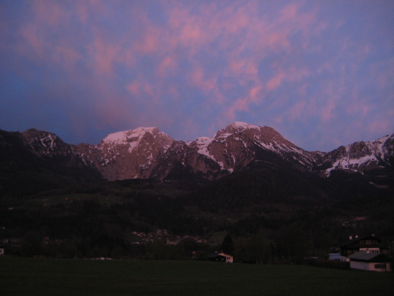 Uma cordilheira com picos nevados e uma aldeia em primeiro plano.