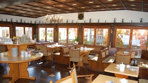 Um restaurante com mesas e cadeiras de madeira, grandes janelas e um candelabro.
