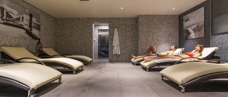 Uma área de spa com cadeiras reclináveis, uma parede revestida de azulejos e uma porta para uma área de chuveiro.