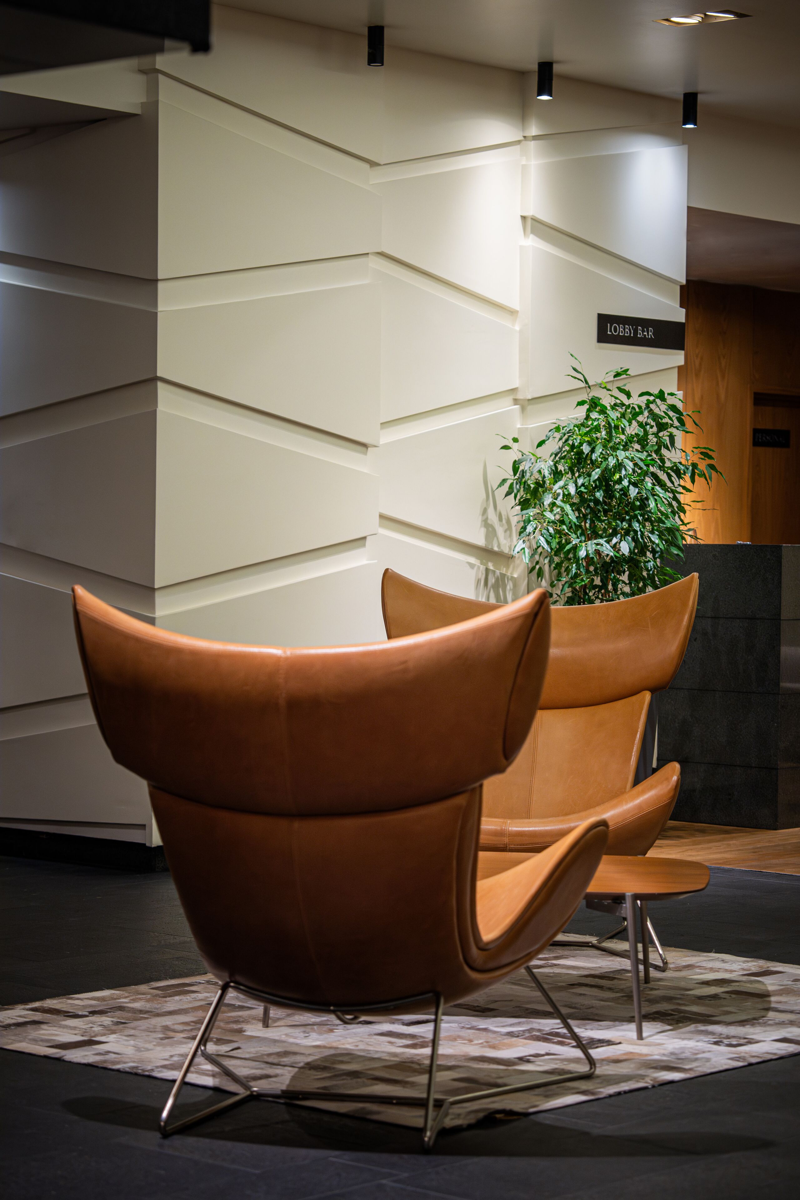 Um hall com assentos modernos, uma placa indicando um bar no hall e uma planta em vaso.