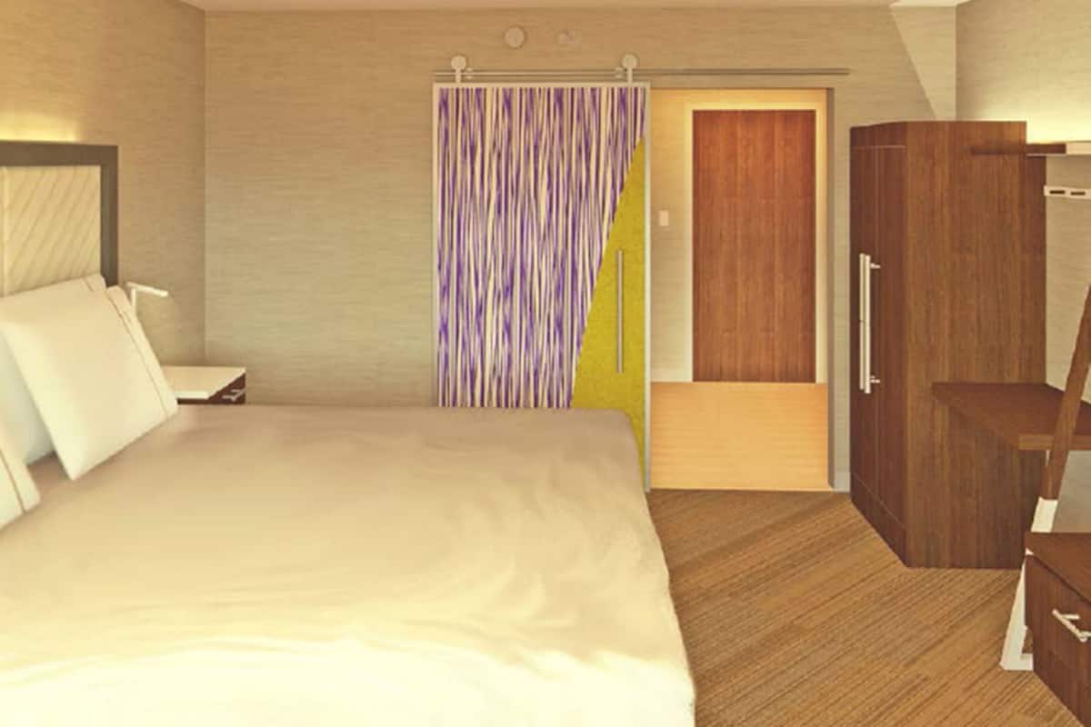 Quarto de hotel com uma cama grande, guarda-roupa de madeira, uma escrivaninha e banheiro com cortina de chuveiro.