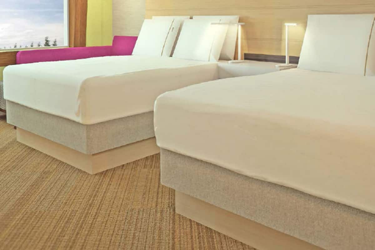 Quarto de hotel com duas camas, uma janela com vista e um abajur na mesa de cabeceira.